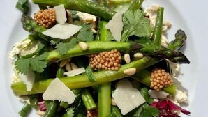 Um prato branco com salada de vegetais verdes, queijo e pinhões.