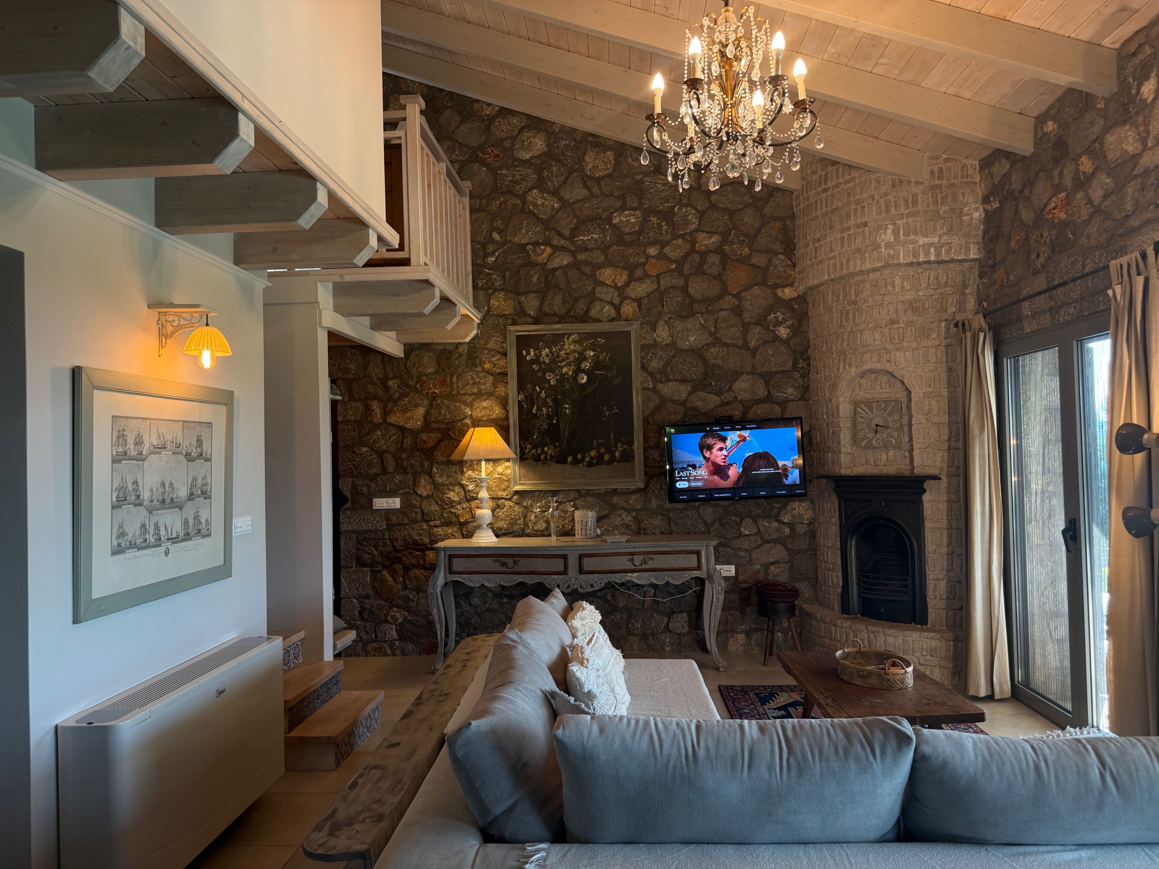 Uma sala de estar com parede de pedra, um candelabro, uma televisão, uma lareira e um sofá.