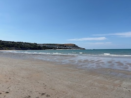 Uma praia com céu claro, mar calmo e uma cidade ao longe.