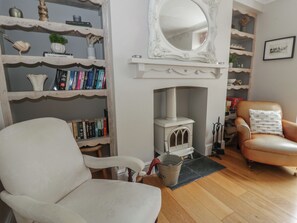 Uma sala de estar com poltrona branca, lareira, estante de livros e espelho.