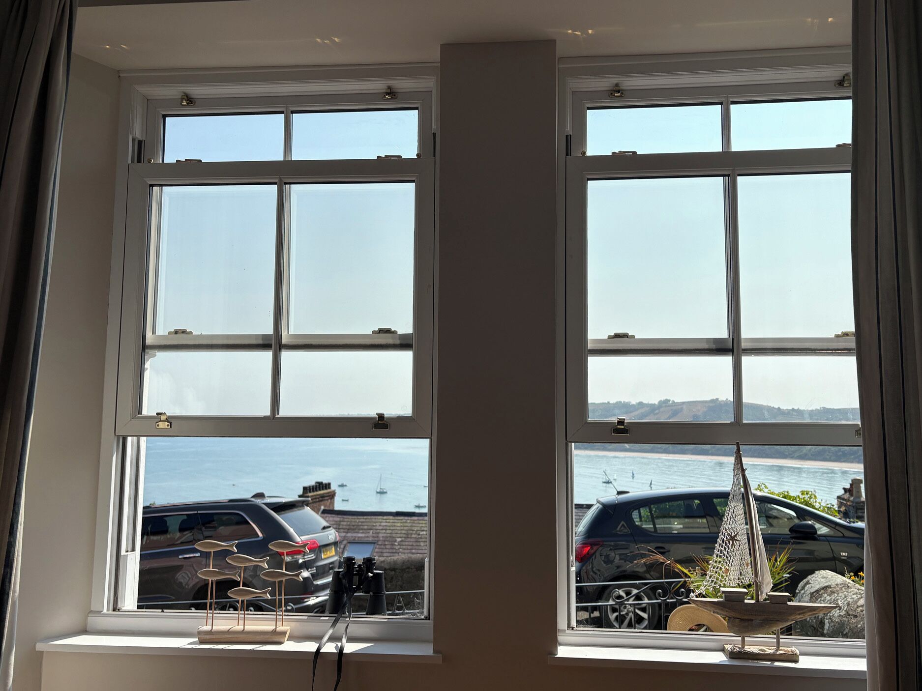 Um quarto com uma janela grande com vista para um corpo de água, um carro estacionado do lado de fora e um pequeno objeto decorativo no parapeito.
