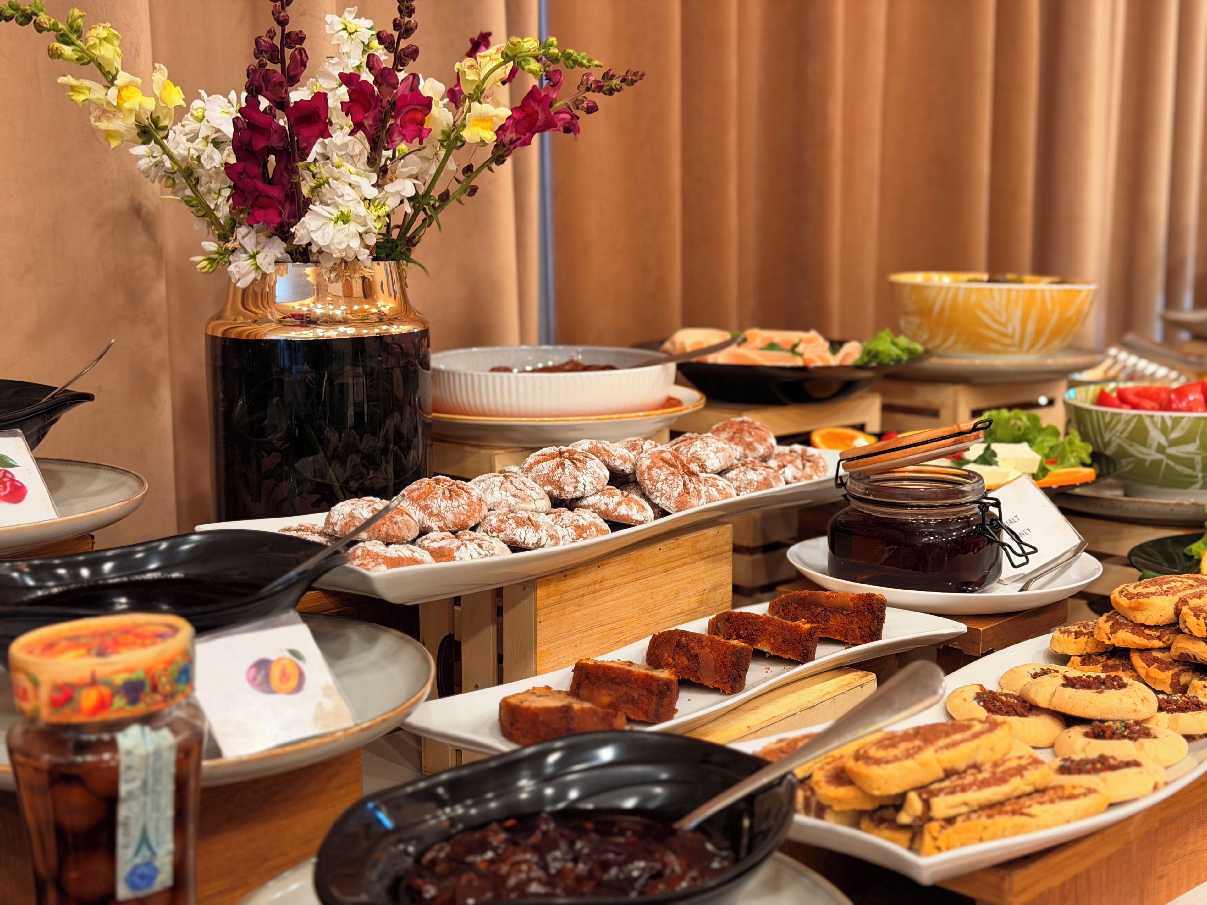 Buffet com diversos alimentos, um vaso de flores e uma vela.