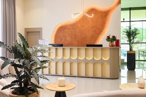 Balcão de recepção com design exclusivo, um vaso de planta e uma área de estar com uma mesa pequena.