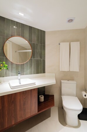 Uma casa de banho moderna com uma pia branca, um espelho redondo, uma sanita e um porta-toalhas.