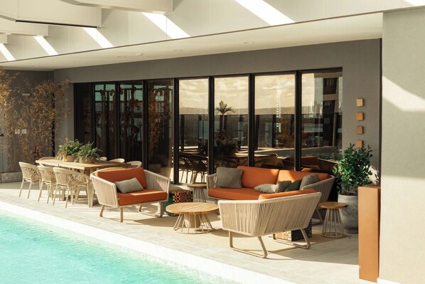 Uma área de estar moderna ao ar livre, com mobiliário de vime, piscina e janelas amplas com vista para a cidade.