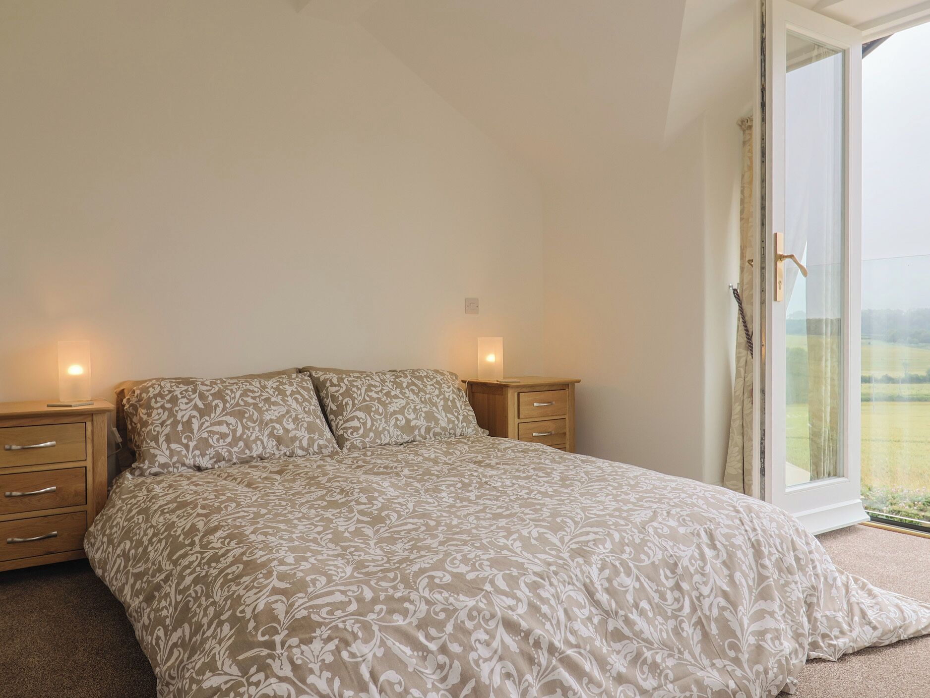 Quarto com uma cama grande, duas mesas de cabeceira, uma janela com cortinas e vista para o exterior.