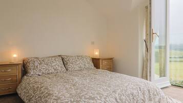 Quarto com uma cama grande, duas mesas de cabeceira, uma janela com cortinas e vista para o exterior.