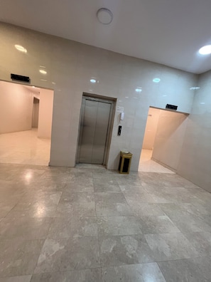 Um hall amplo com piso de mármore, um elevador e uma lixeira.