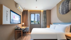 Quarto de hotel com cama, escrivaninha, cadeira, televisão e vista para edifícios.
