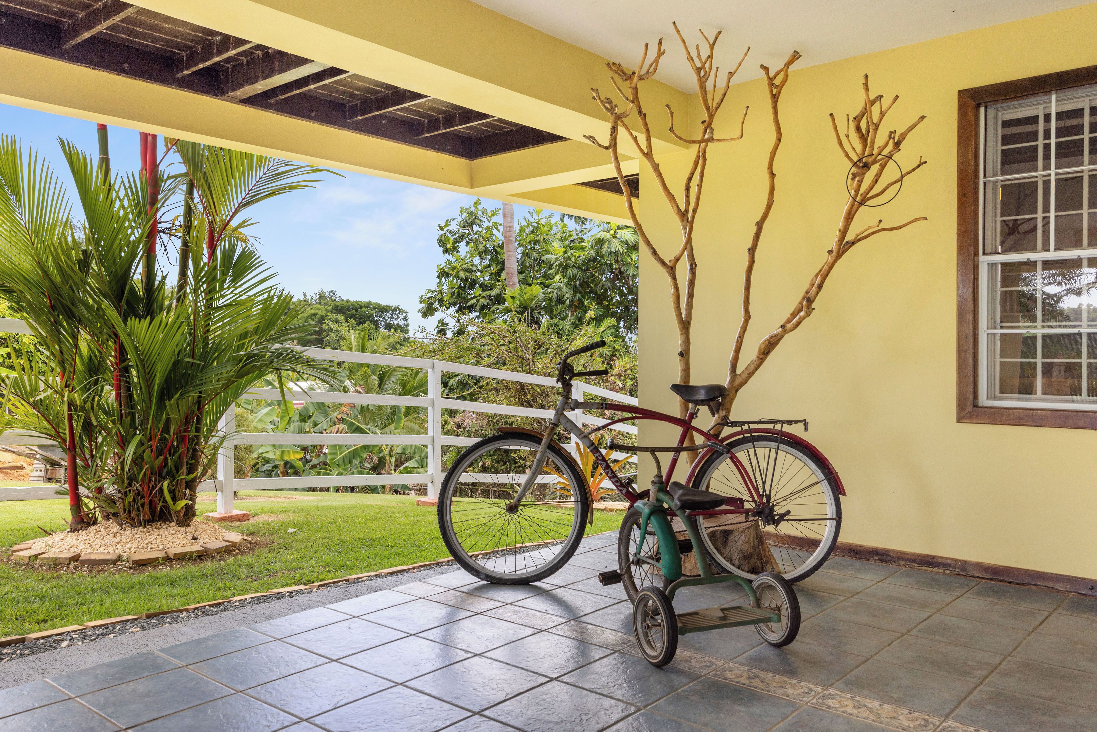 Uma área de varanda coberta com uma bicicleta, cerca branca e vista para o exterior.