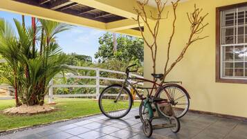 Uma área de varanda coberta com uma bicicleta, cerca branca e vista para o exterior.