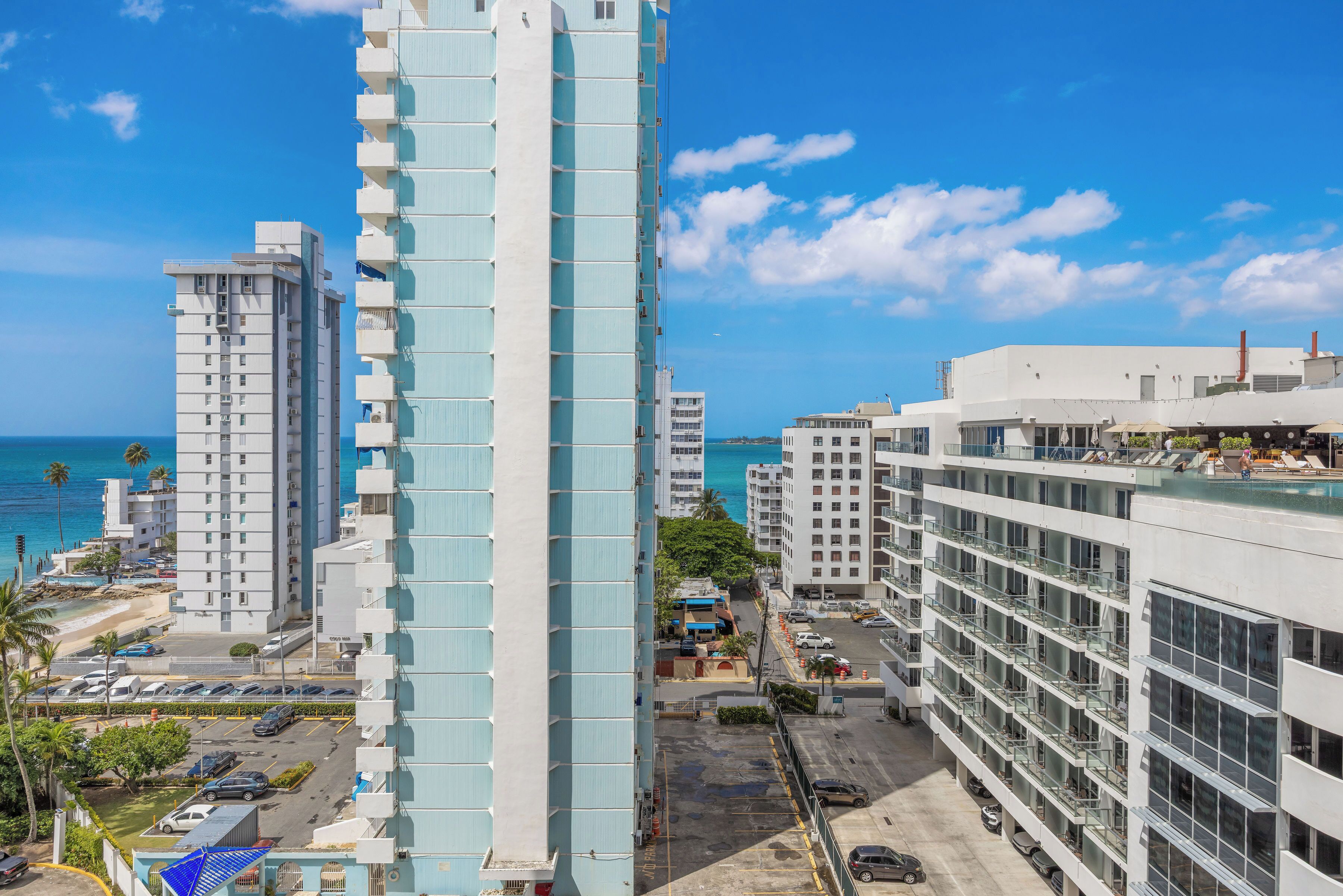 Um hotel alto com vista para o oceano, área de estacionamento e edifícios próximos.