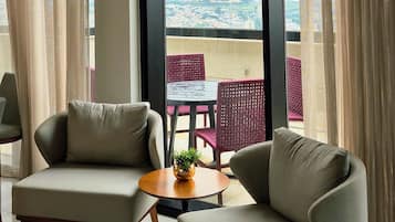 Uma sala de estar moderna com uma janela grande, dois sofás, uma mesa pequena e vista para a cidade.