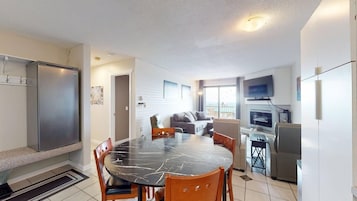Cozinha moderna com geladeira embutida, área de jantar com mesa de mármore e sala de estar com sofá e televisão.