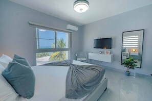 Quarto moderno com uma cama grande, televisão, espelho e planta em vaso.