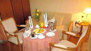 Mesa posta com pratos, copos e uma tigela de frutas, rodeada por cadeiras.