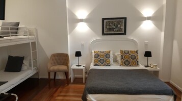 Uma cama de solteiro com uma cadeira e mesas de cabeceira, uma cama com almofadas estampadas e um aplique de parede.