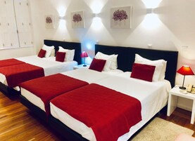 Quarto de hotel com duas camas, cada uma com roupa de cama branca e detalhes vermelhos, uma mesa de cabeceira com abajur e obras de arte nas paredes.