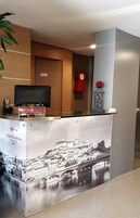 Bancada de recepção de hotel com monitor, relógio e um objeto decorativo na parede.