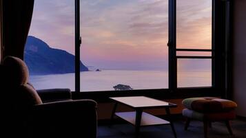Quarto com uma grande janela com vista para um corpo de água e uma terra distante, um sofá, uma mesa pequena e um banquinho.