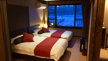 Quarto de hotel com duas camas, uma janela e vista para o mar, e um ar condicionado.