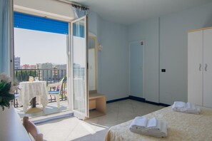 Quarto de hotel com varanda, cama com toalhas, guarda-roupa e pequena mesa com cadeira.