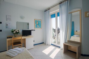 Quarto de hotel com cama, escrivaninha com computador, televisão, espelho e varanda com cortinas.