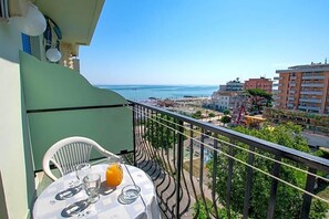 Uma varanda com mesa, cadeiras e vista para o mar e edifícios.