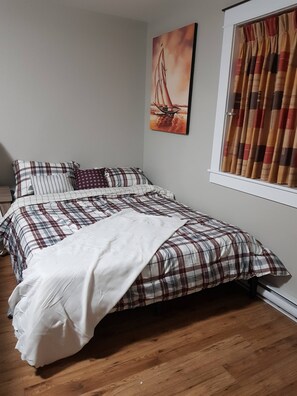 Um quarto com uma cama, um quadro e uma janela com cortinas.