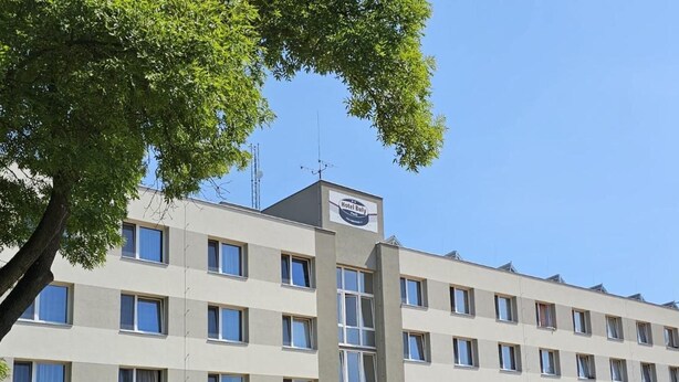 Um edifício de hotel com vários andares, fachada plana, inúmeras janelas e uma placa indicando que é um hotel.