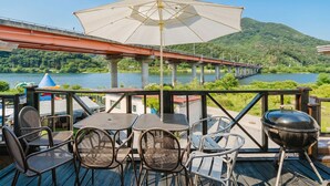 Um terraço com área de estar externa, churrasqueira e vista para uma ponte sobre o rio.