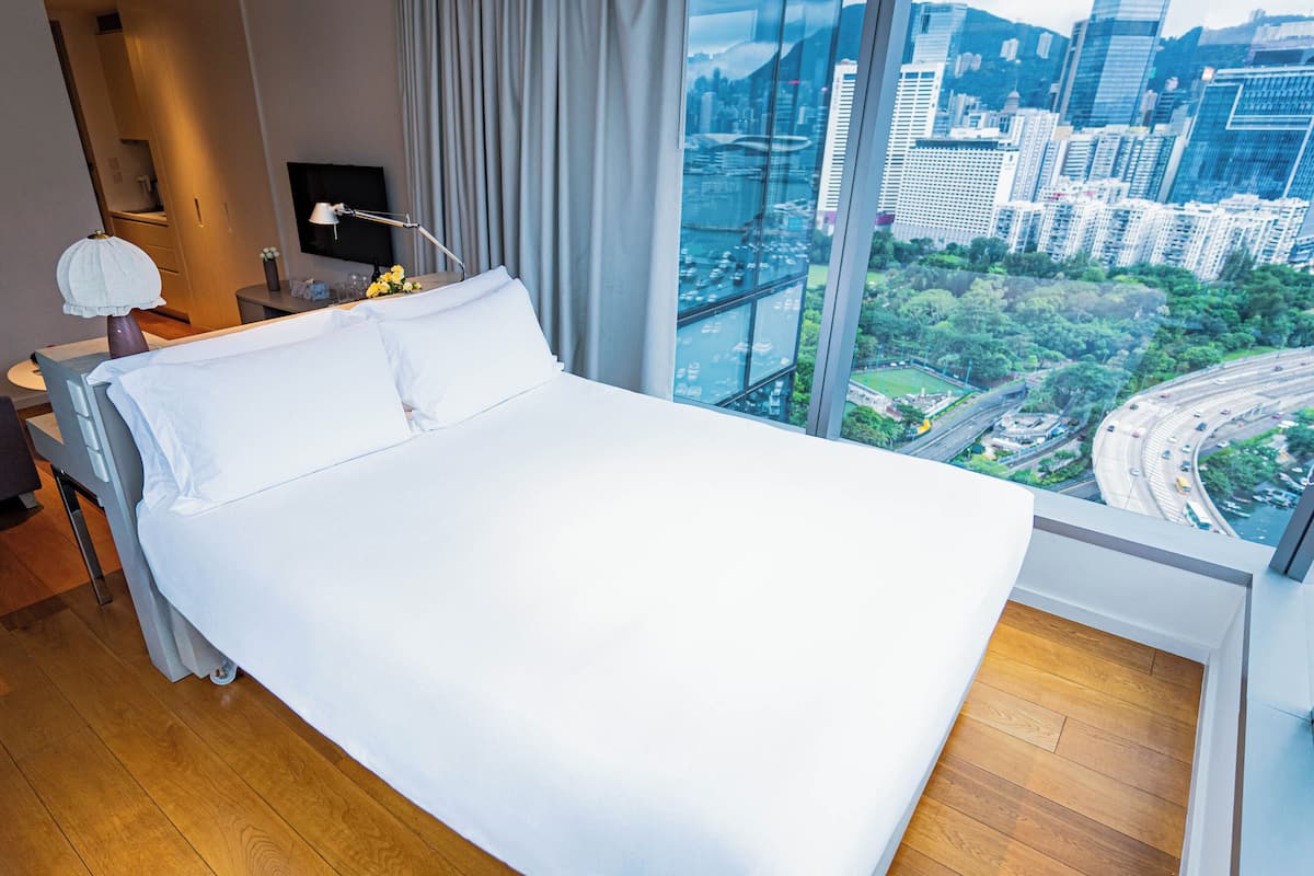 Quarto de hotel com cama, escrivaninha, cadeira, TV e uma grande janela com vista para a cidade.