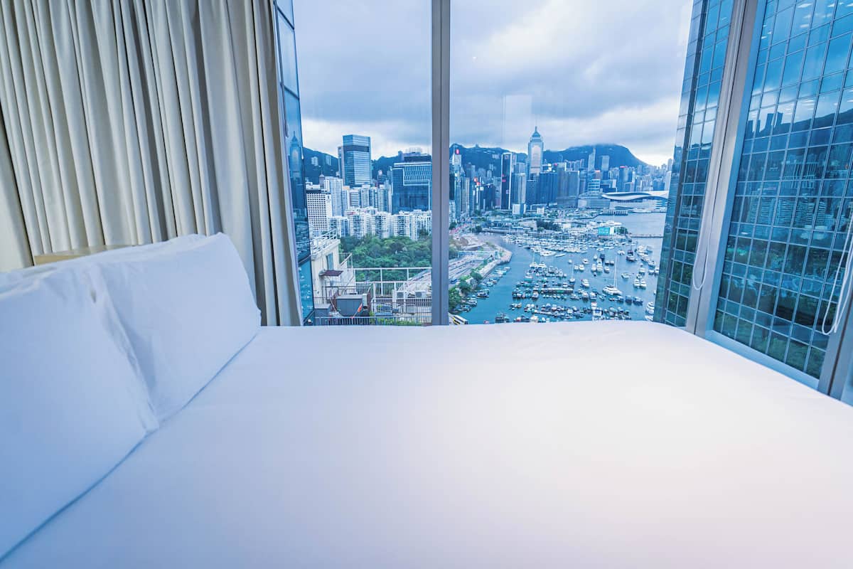 Quarto de hotel com uma cama grande, vista para a paisagem urbana e uma parede de vidro.