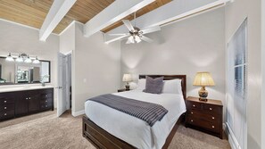 Quarto com cama, mesas de cabeceira, ventilador de teto, um espelho grande e banheiro com toucador.