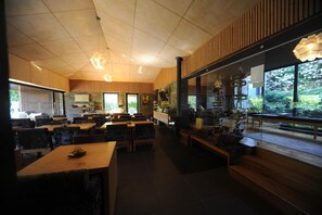 Interior de restaurante moderno com painéis de madeira, detalhes em pedra e grandes janelas com vista para o verde.