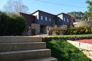 Uma casa moderna de dois andares com uma escadaria de pedra que leva à entrada, cercada por um jardim bem cuidado.