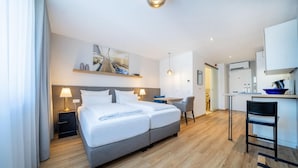 Quarto de hotel moderno com cama de casal, escrivaninha e cozinha compacta.