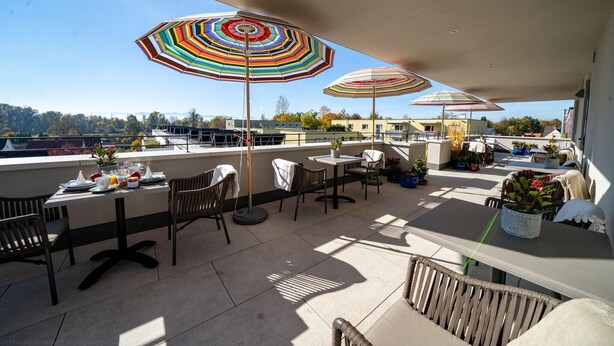 Terraço no telhado com área de estar ao ar livre, guarda-sóis listrados e vista para a paisagem urbana.