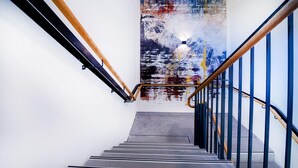 Uma escadaria com design moderno, corrimãos de metal e um quadro abstrato grande na parede.