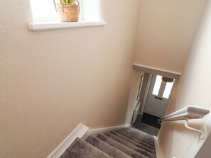 Uma escadaria coberta de carpete com um corrimão branco, uma pequena janela com uma cesta e uma porta no topo.