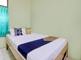 Uma cama de solteiro com colcha branca e azul, duas almofadas com padrões geométricos e uma cortina verde-água.