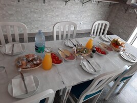 Uma mesa de jantar posta com pratos, talheres e diversos alimentos, incluindo pão, tomates e uma garrafa de suco.