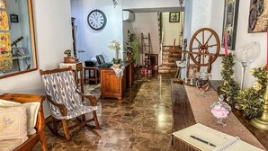 Uma sala ampla com uma mesa de centro de madeira, uma poltrona estampada, um relógio grande e uma roda de madeira rústica.