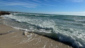 Uma praia com ondas, céu claro e uma linha de costa distante.