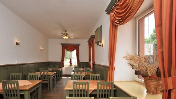 Um restaurante com mesas e cadeiras de madeira, um ventilador de teto e uma janela com cortinas.