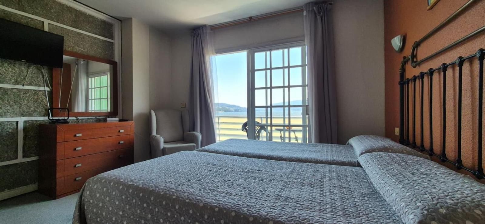 Quarto de hotel com duas camas, penteadeira, uma cadeira e uma janela grande com vista.