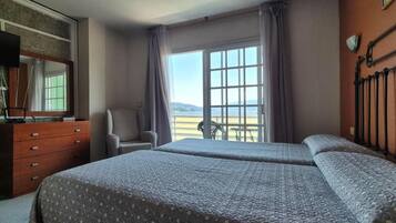Quarto de hotel com duas camas, penteadeira, uma cadeira e uma janela grande com vista.