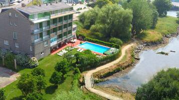 Um hotel com vários andares, piscina e vista para o rio.
