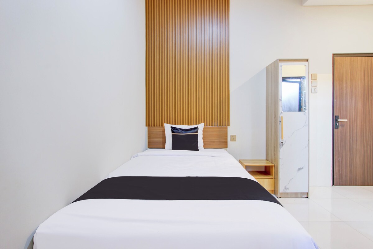 Quarto de hotel com cama, cabeceira de madeira, mesa de cabeceira, guarda-roupa e uma porta.