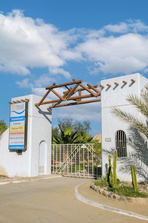 Um edifício branco com um arco de madeira, uma placa indicando os serviços e um cacto em primeiro plano.